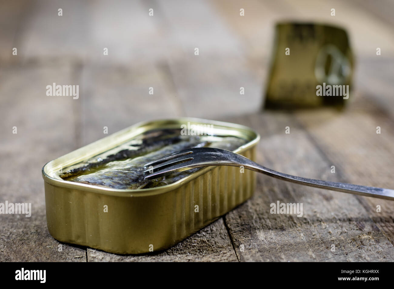 A tin can of fish on a wooden kitchen table. Next to the can fork ...