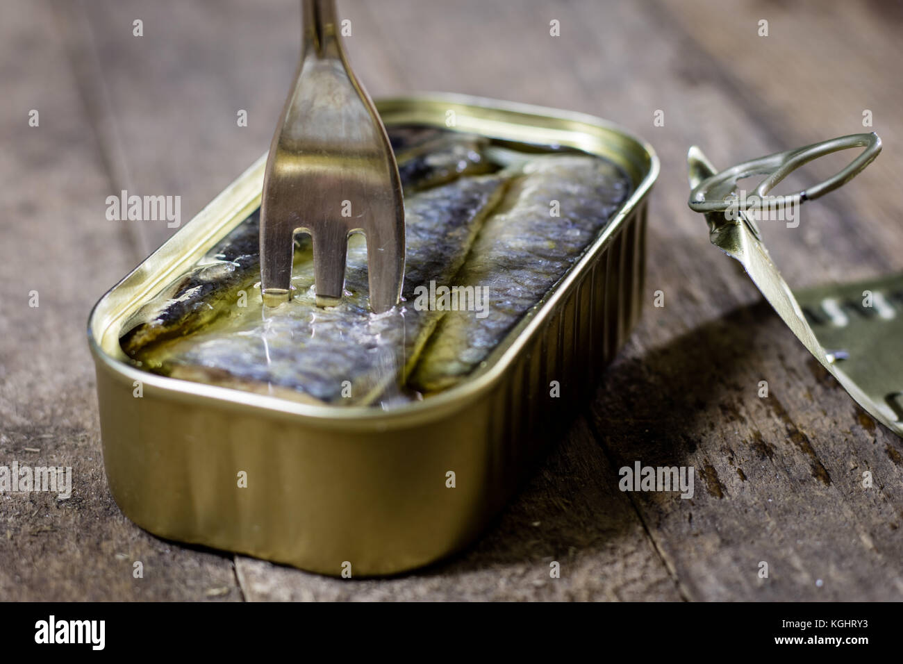 A tin can of fish on a wooden kitchen table. Next to the can fork ...