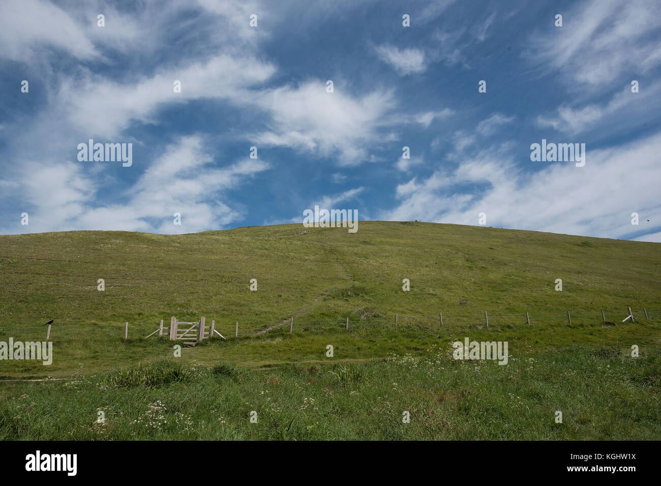 English landscape with green hill and wooden gates and clouded sky ...