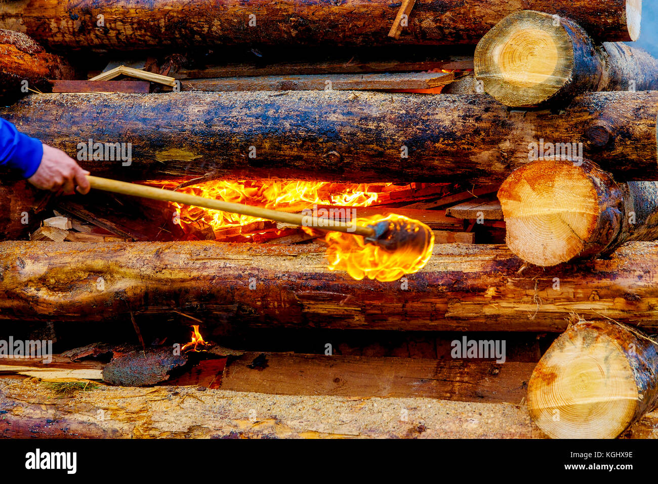 setting big bonfire made of logs on fire with torch Stock Photo - Alamy