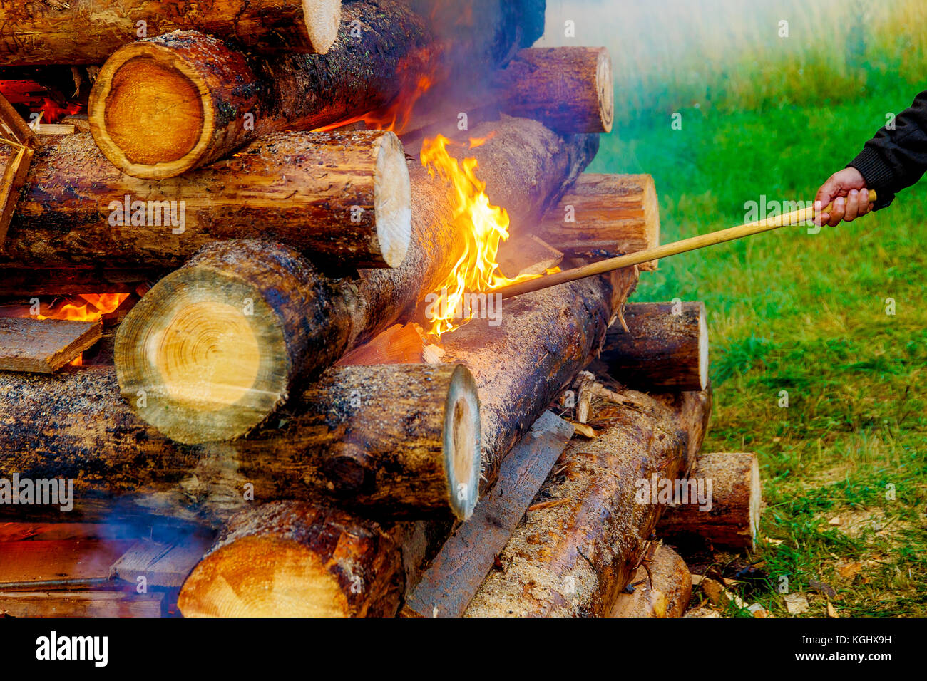 setting big bonfire made of logs on fire with torch Stock Photo - Alamy