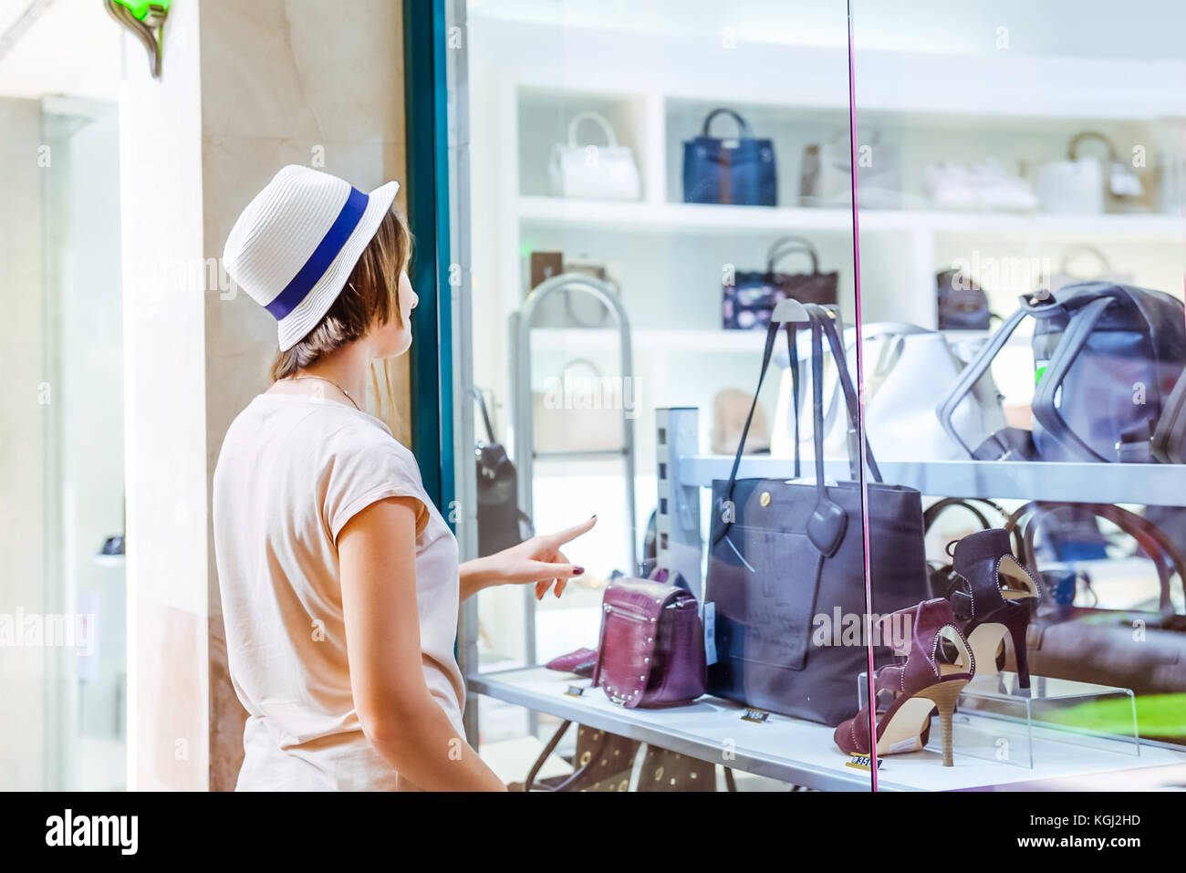 Young doubting girl looking at shop window with shoes and bags in ...