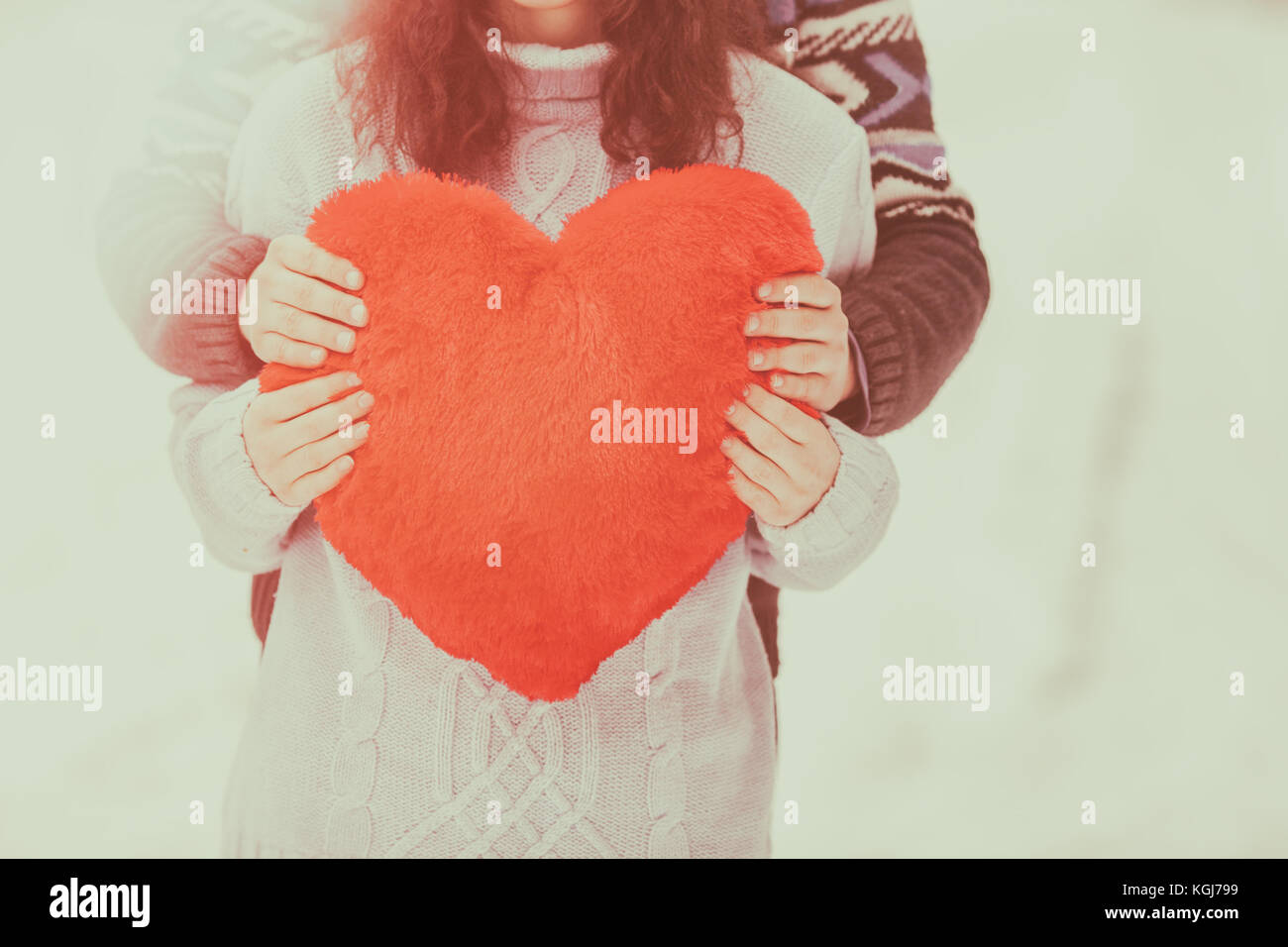Young couple wearing sweaters with heart hugging outdoors in winter ...