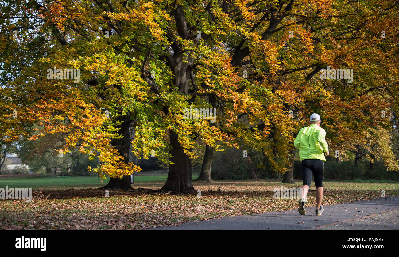 A man running by trees with autumnally coloured foliage near the river ...