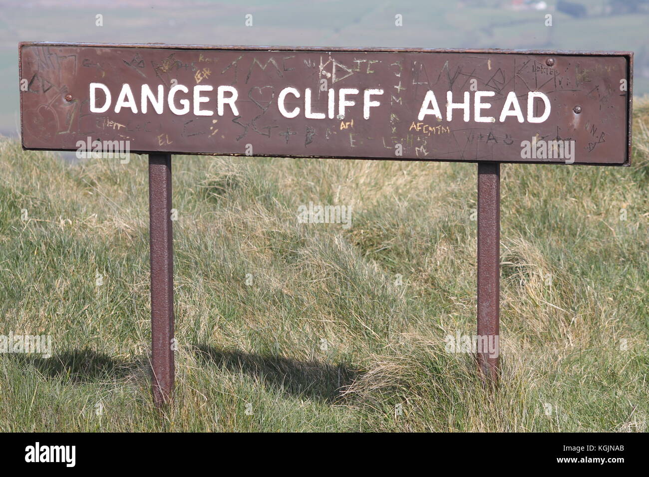 Warning sign reading “Danger Cliff Ahead” on grassy land, alerting ...