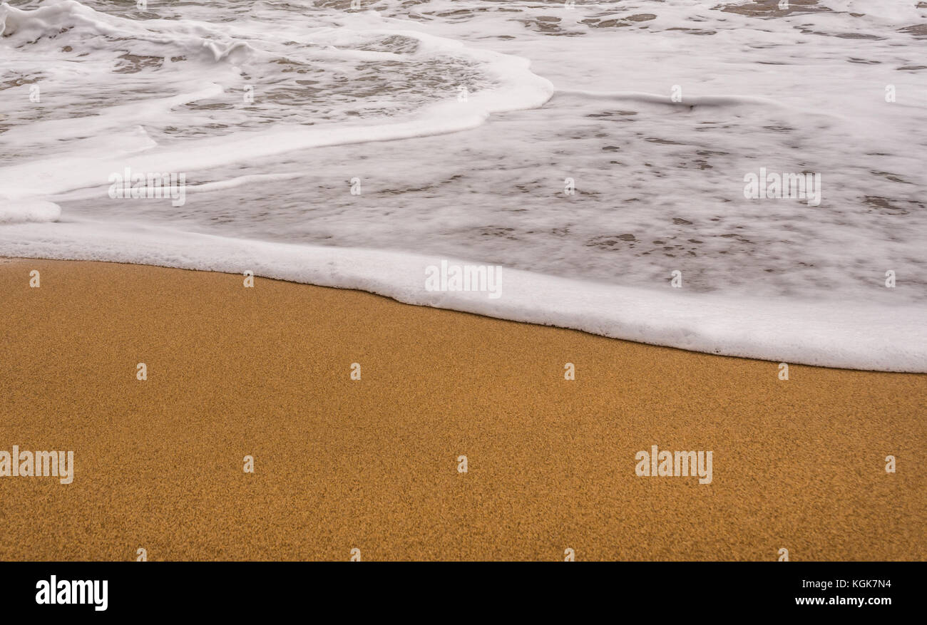 A close up of frothy waves on a stormy day against the golden sandy ...