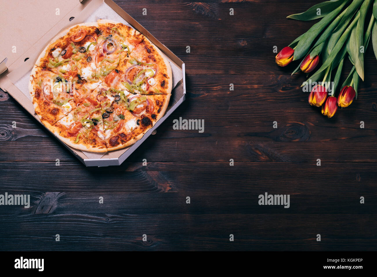 Pizza in a box and a bouquet of tulips on a wooden table top view Stock ...
