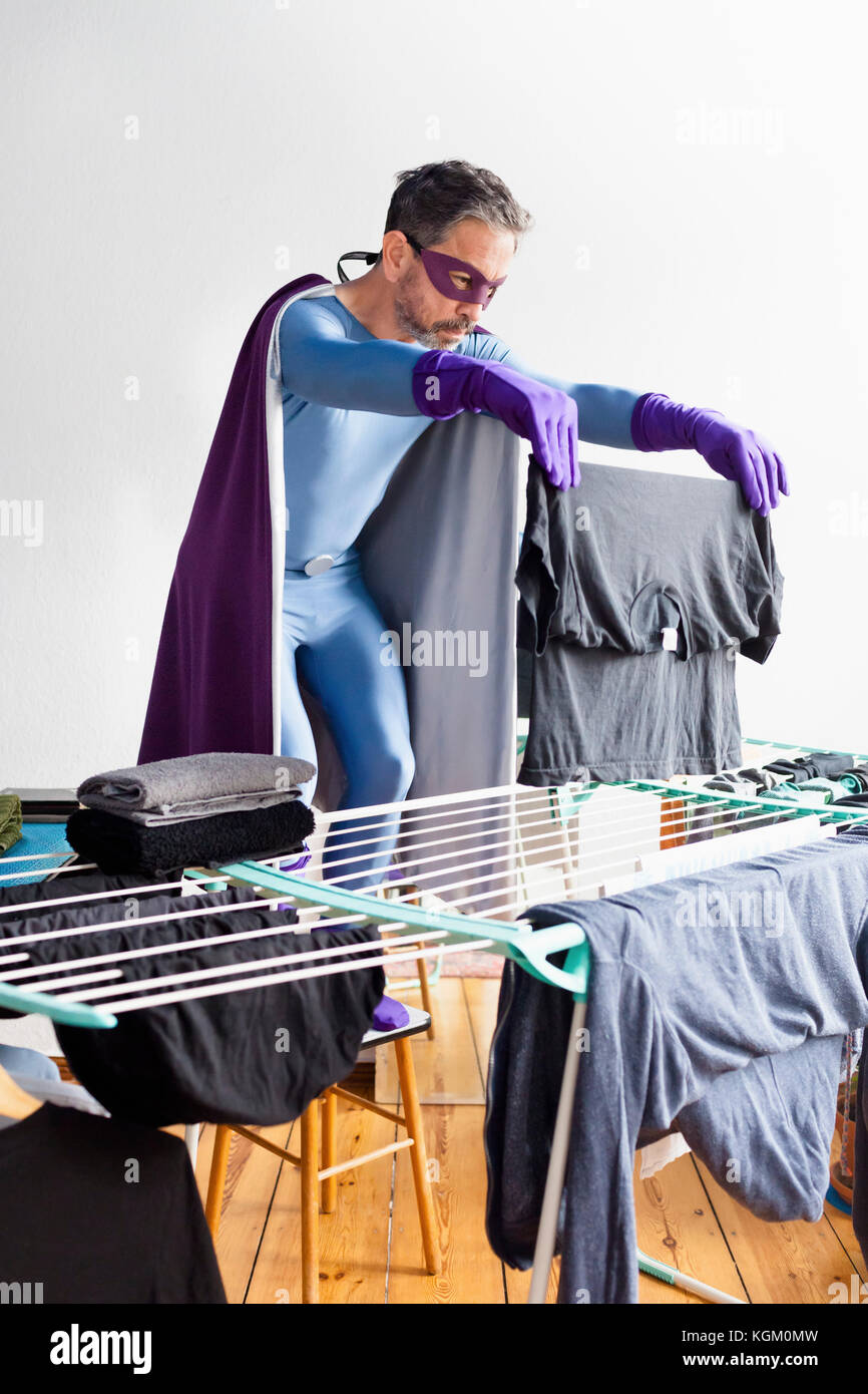 Mature superhero drying laundry on rack against white wall Stock Photo ...