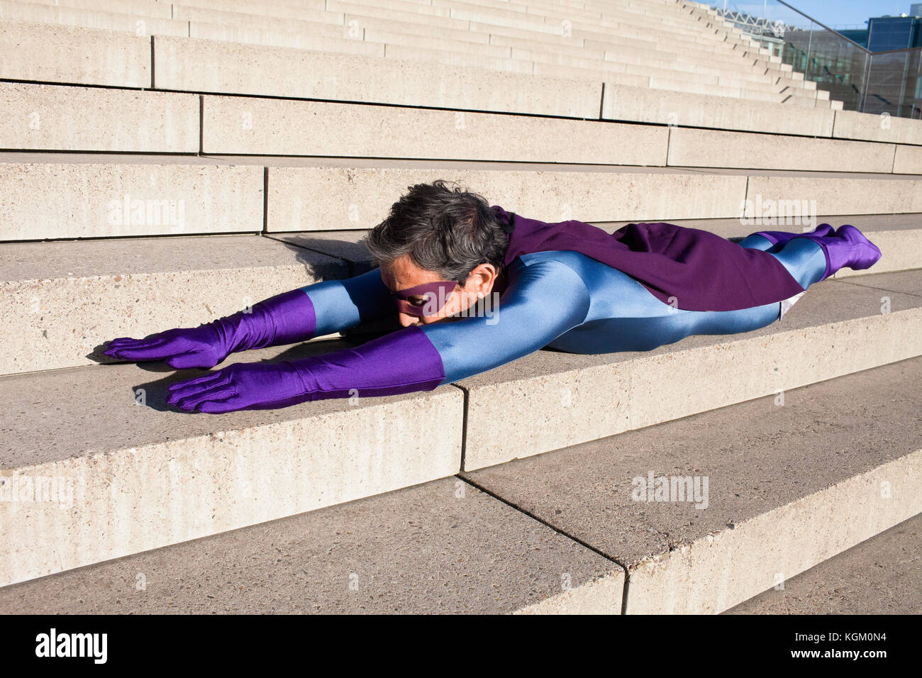 Side view of man dressed as superhero lying on steps Stock Photo - Alamy