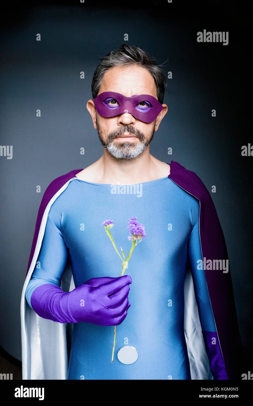 Portrait of man dressed as superhero holding flower against gray ...