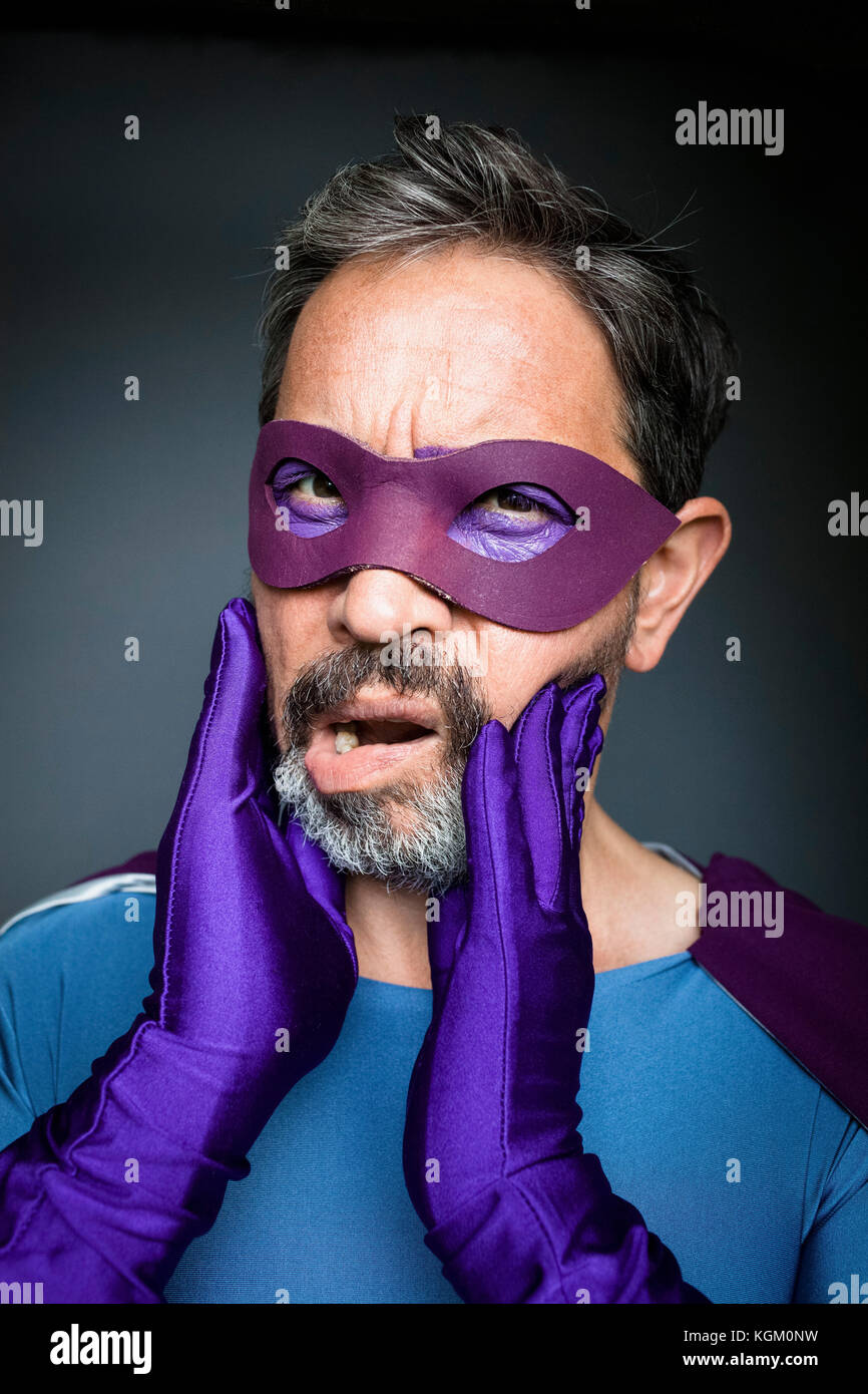 Portrait of superhero with hands on cheeks against gray background ...
