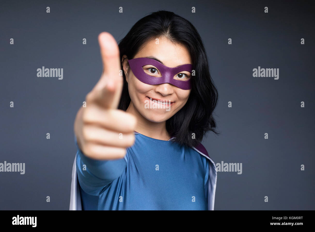 Portrait of smiling female superhero pointing against gray background ...