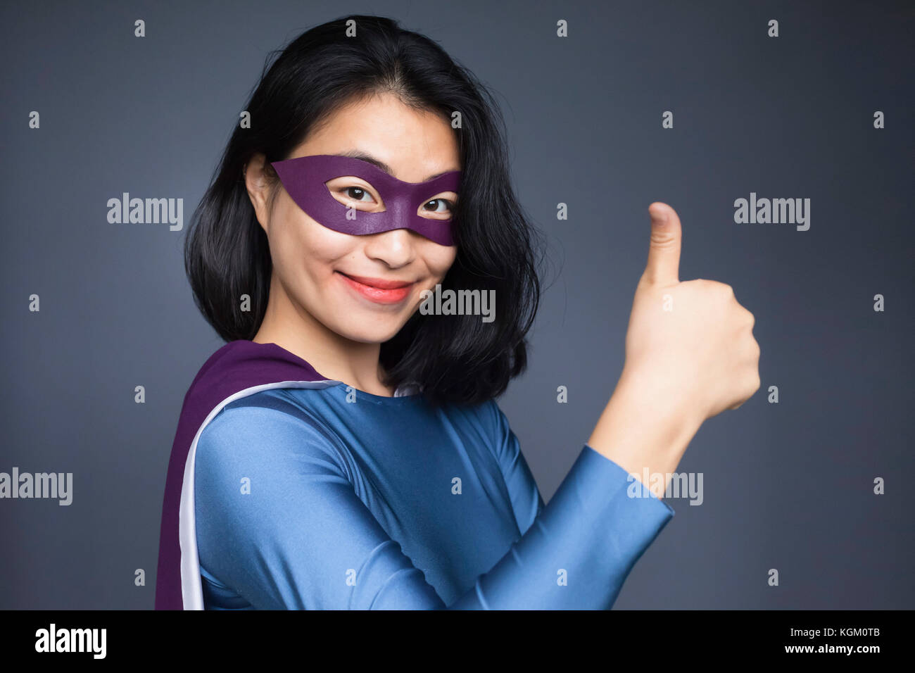 Portrait of confident female superhero gesturing thumbs up against gray ...