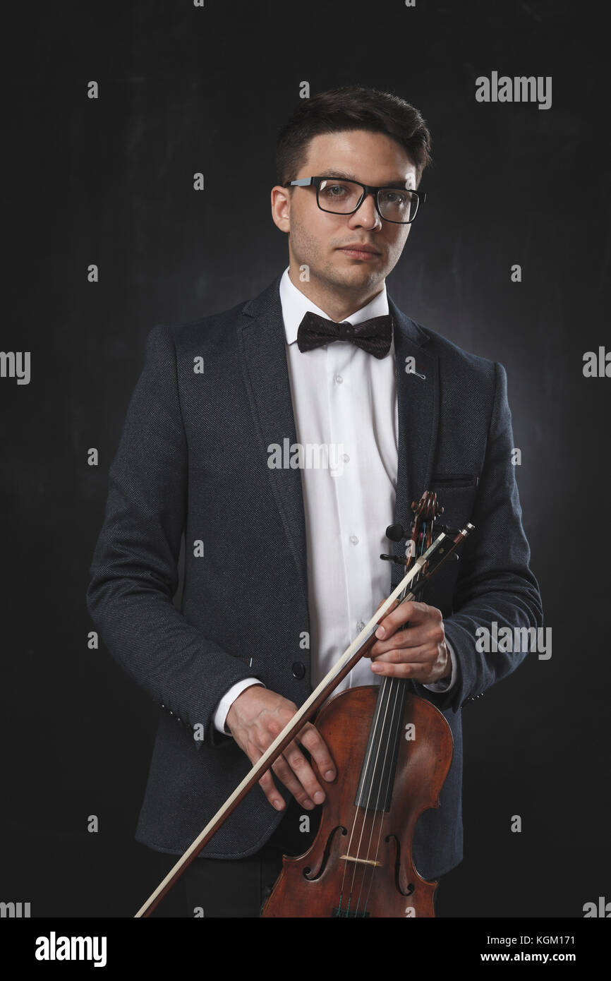 Portrait of confident young man holding violin while standing against ...