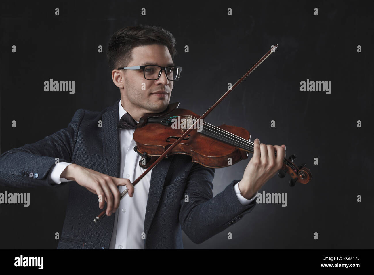 Smiling handsome violinist playing violin against black background ...