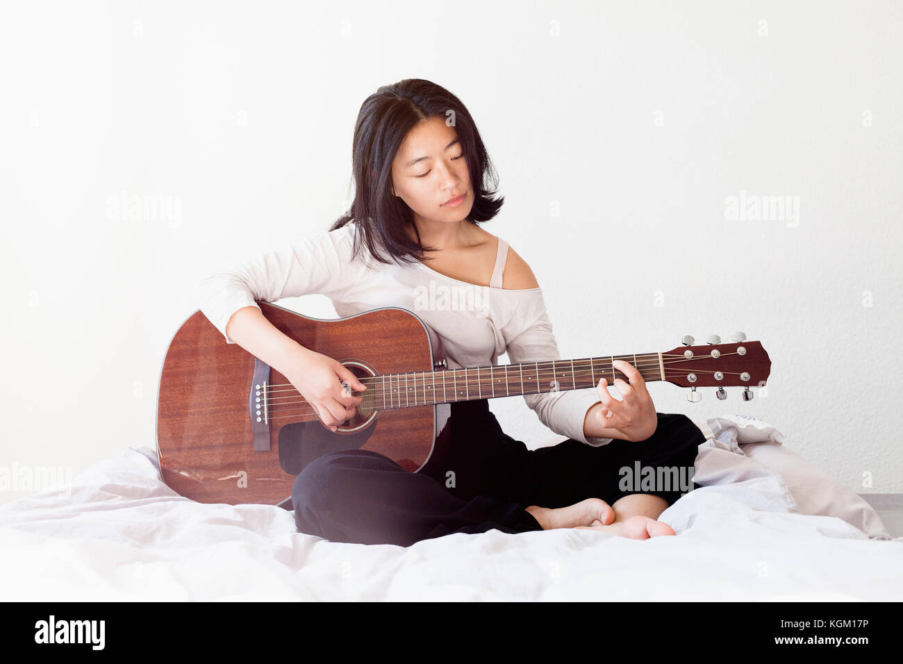 Young woman playing guitar while sitting on bed at home Stock Photo - Alamy