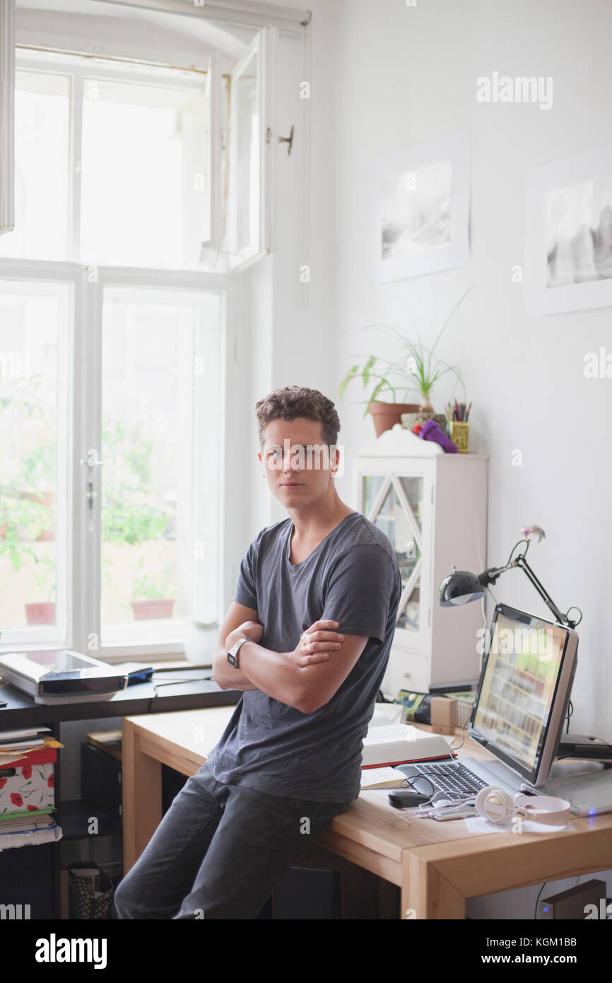 Portrait of handsome man leaning with arms crossed on table at home ...