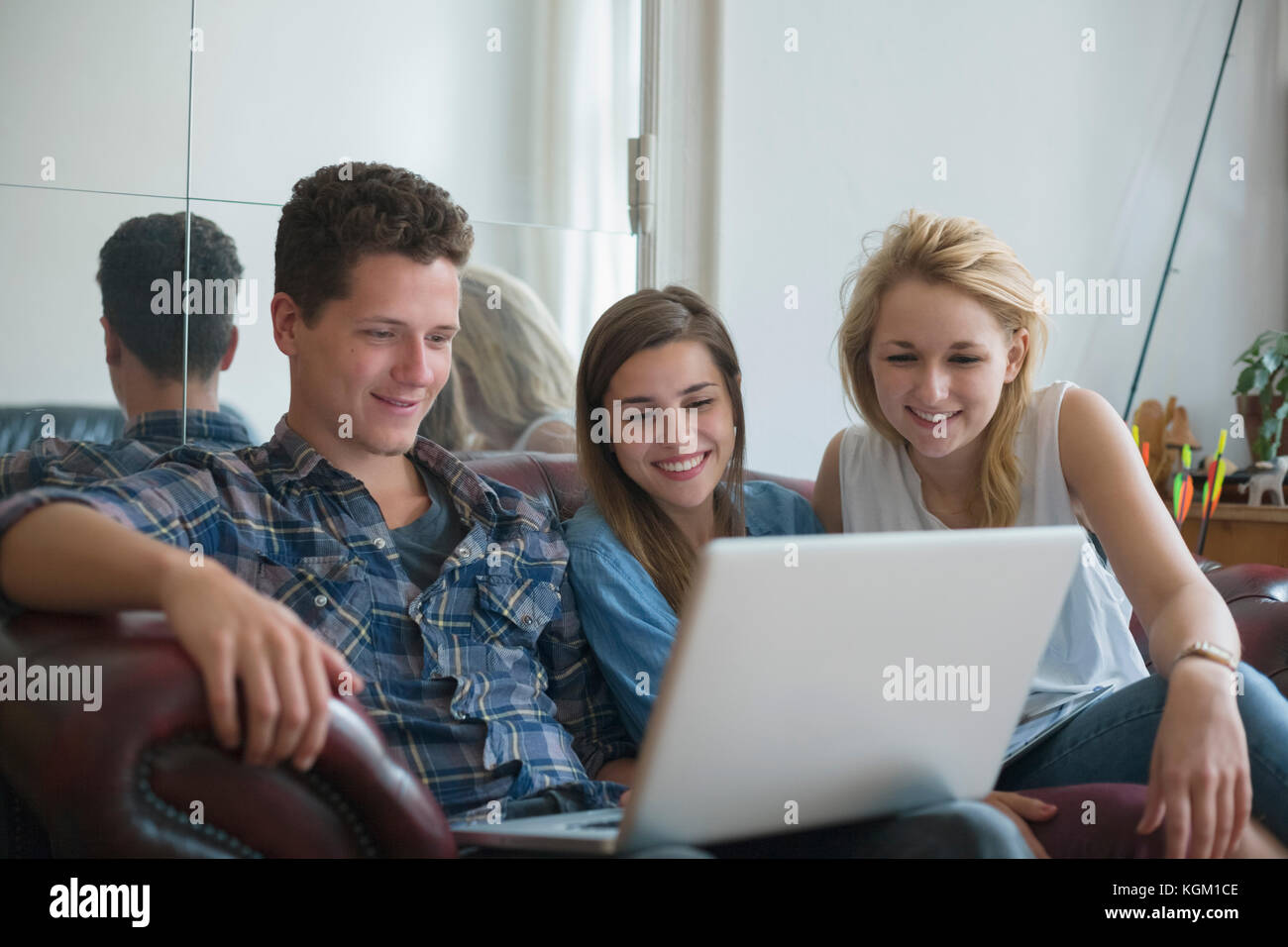 Smiling young friends using laptop while sitting on sofa at home Stock ...