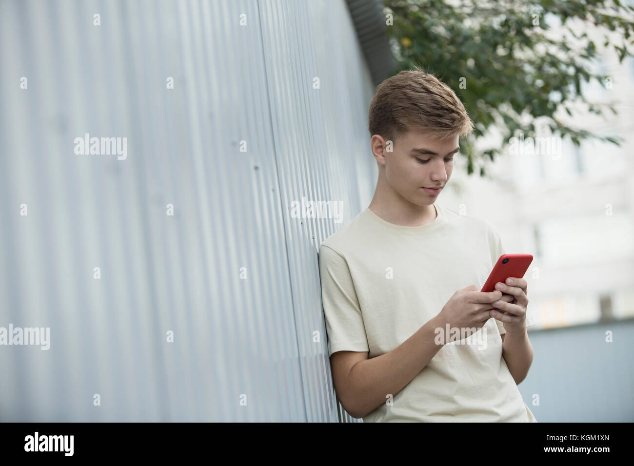 Tilt image of teenage boy using mobile phone while leaning on metallic ...