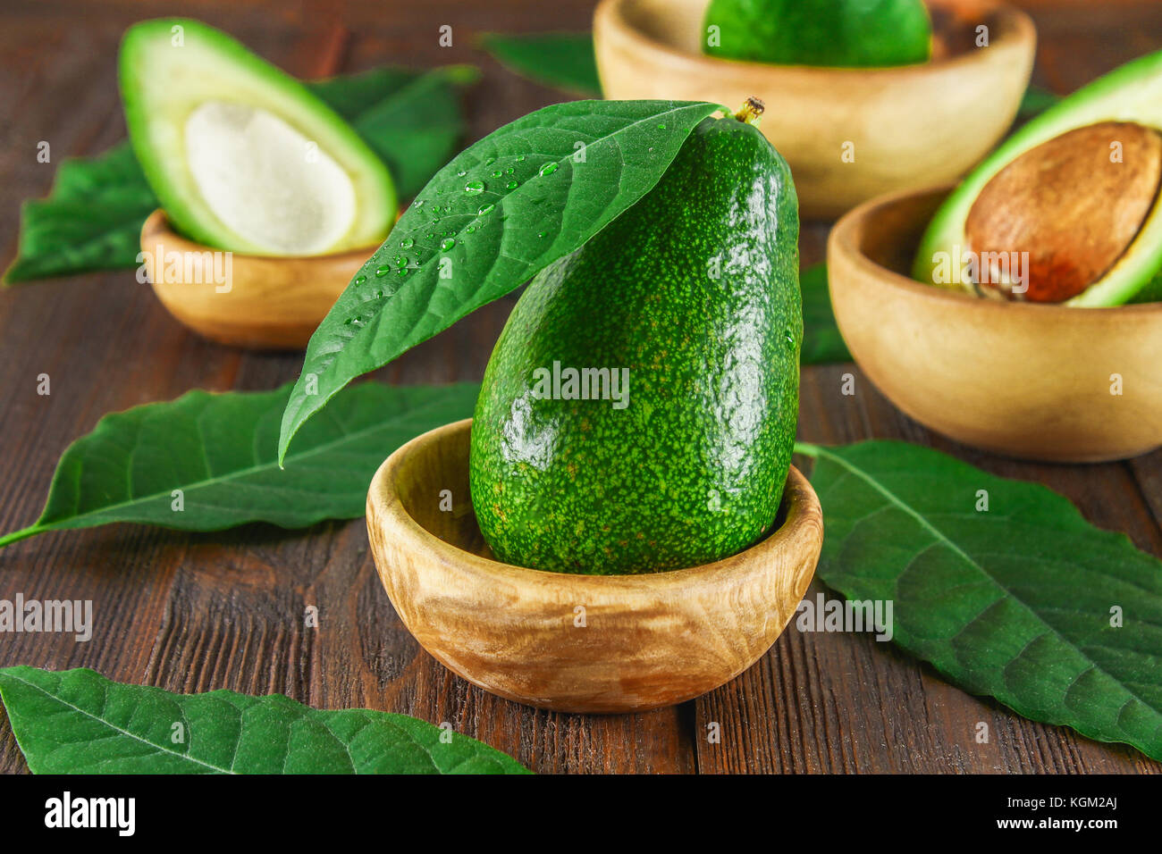 Green raw ripe cut and whole avocado fruits with stone lie in wooden ...