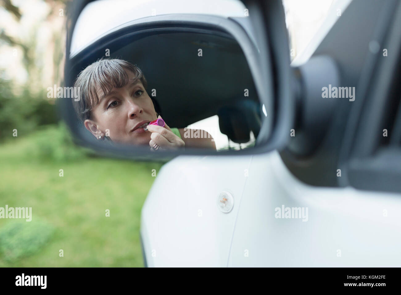 Woman applying lipstick while looking at side-view mirror of car Stock ...