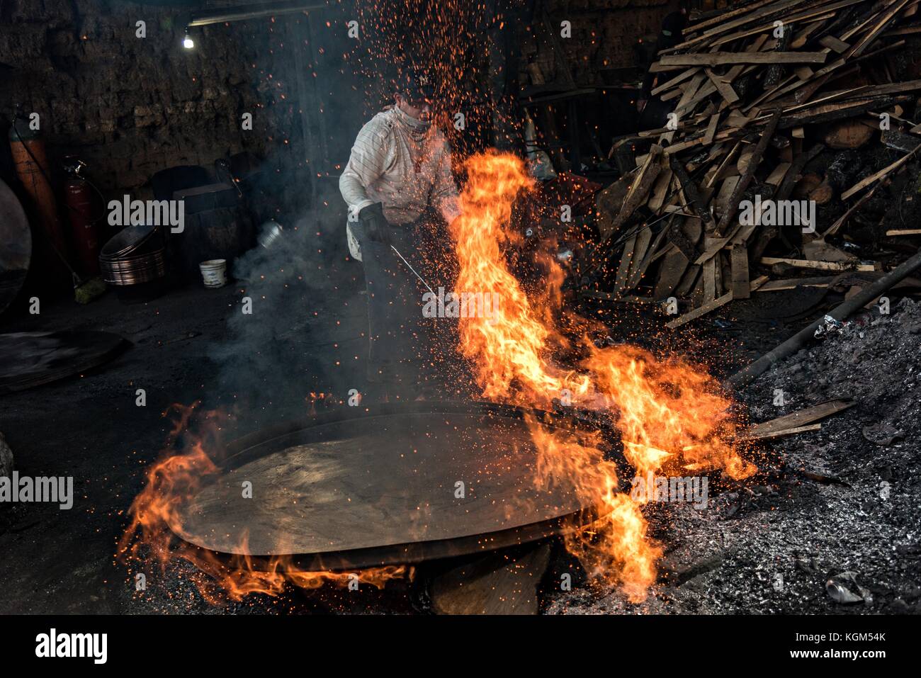 An indigenous Purepecha worker works a copper pan on an open forge to ...