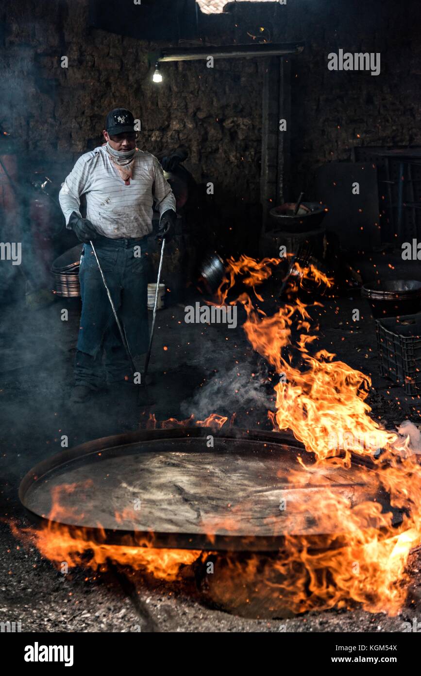 An indigenous Purepecha worker works a copper pan on an open forge to ...