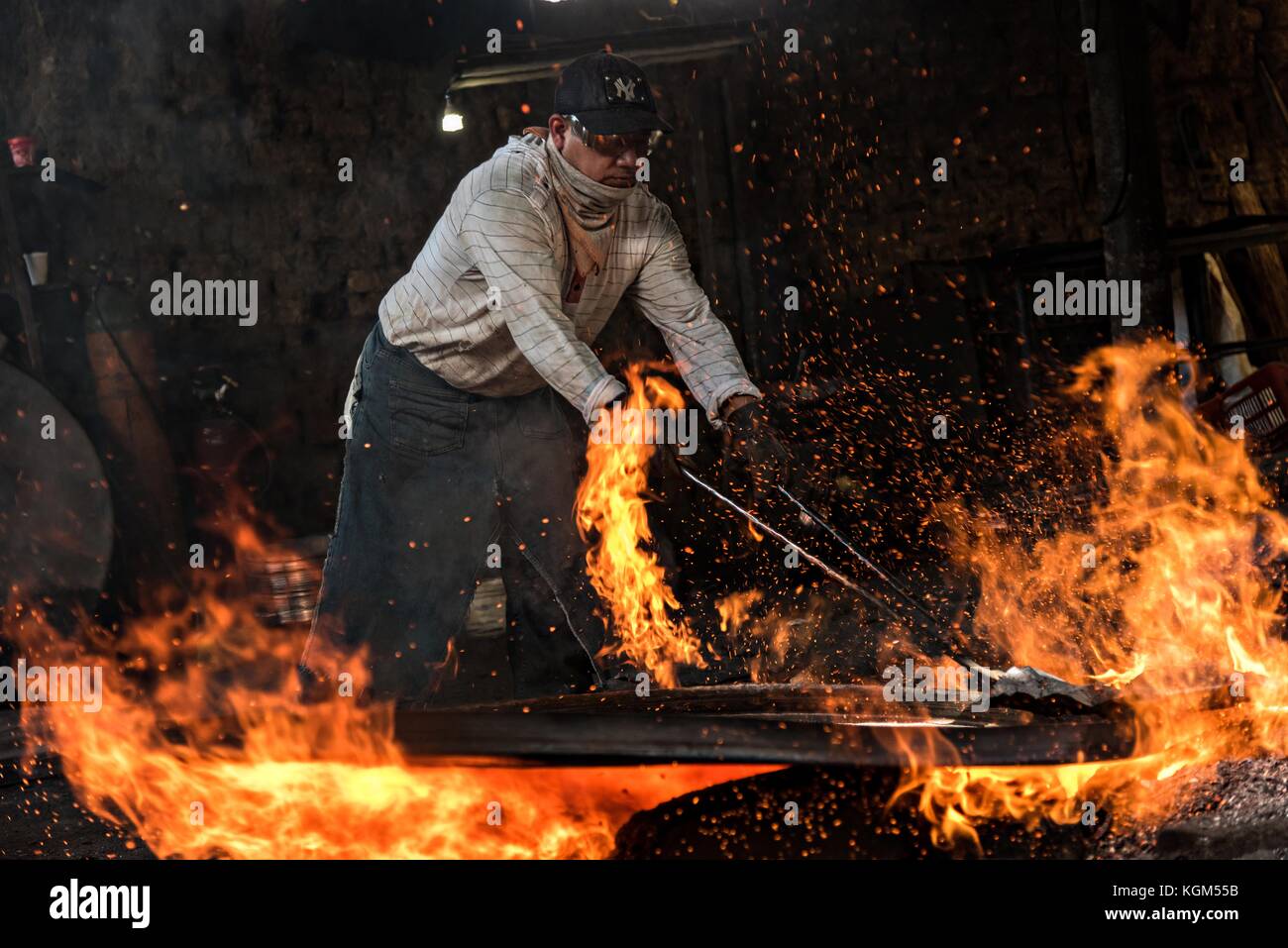 An indigenous Purepecha worker works a copper pan on an open forge to ...