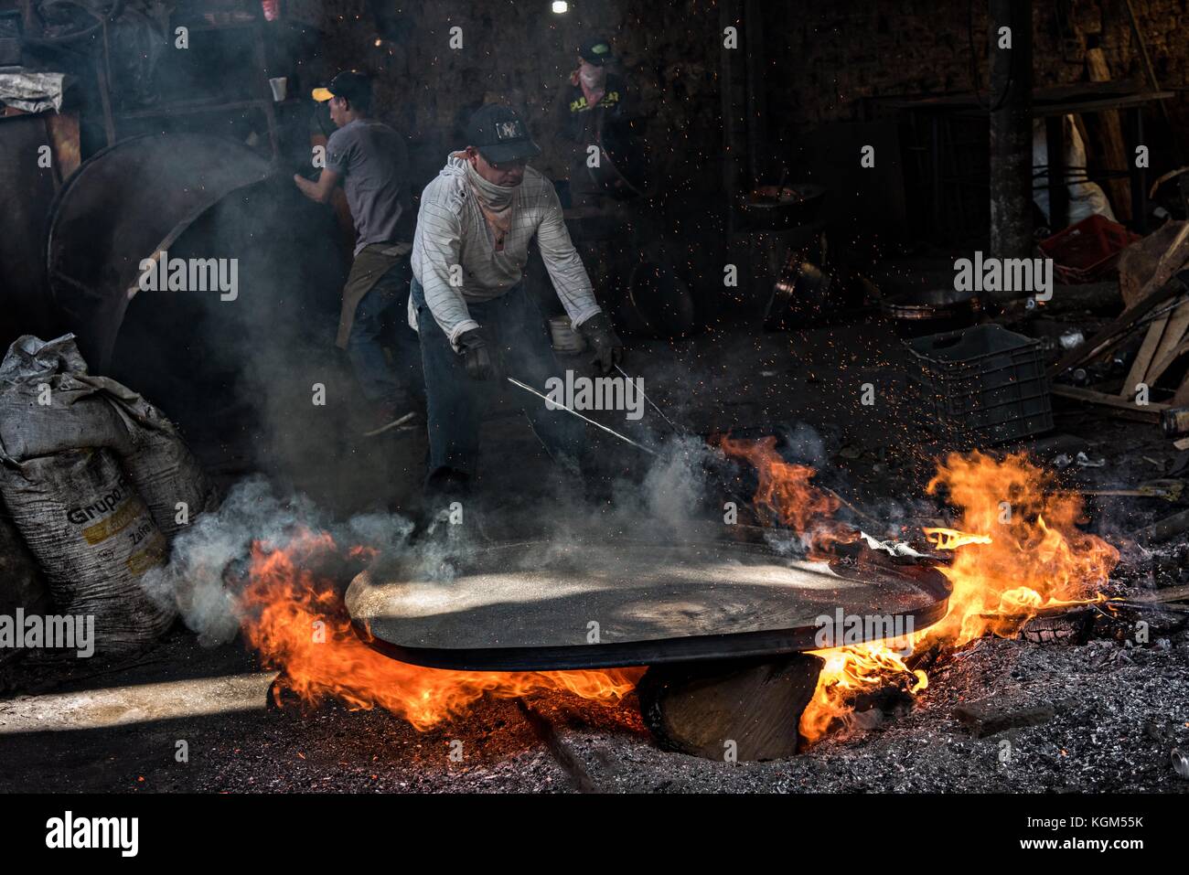 An indigenous Purepecha worker works a copper pan on an open forge to ...