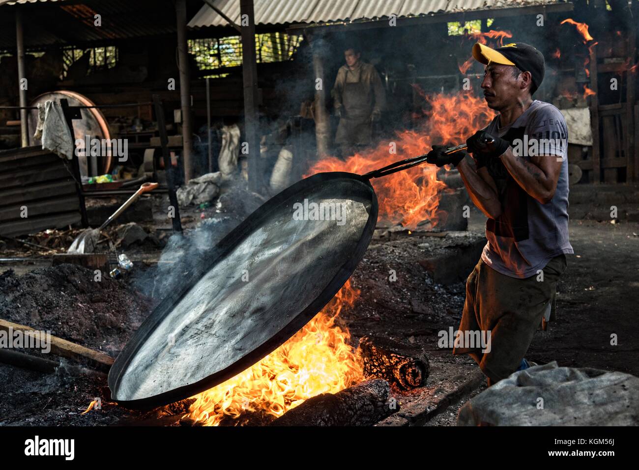 An indigenous Purepecha worker works a copper pan on an open forge to ...