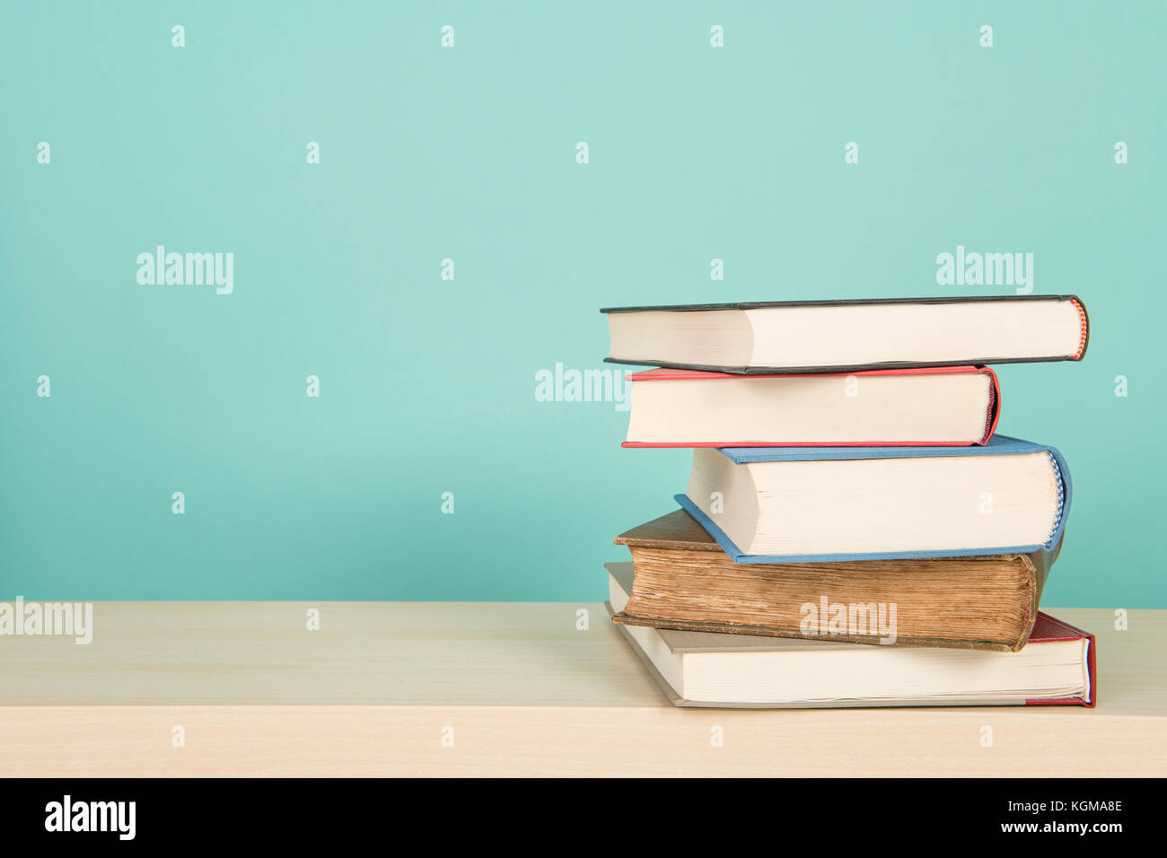 Staple of 5 books lying down on a wooden shelf on a blue background ...
