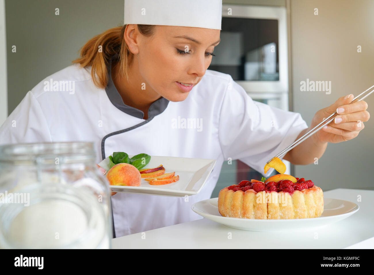 Pastry chef in professional kitchen decorating raspberry cake with ...