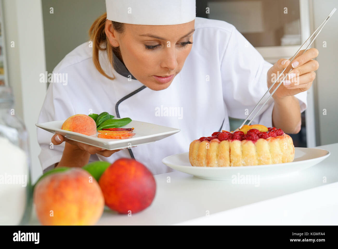 Pastry chef in professional kitchen decorating raspberry cake with ...