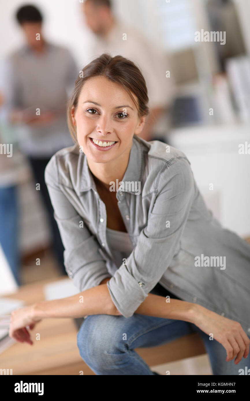 Portrait of business girl sitting on table in office Stock Photo - Alamy