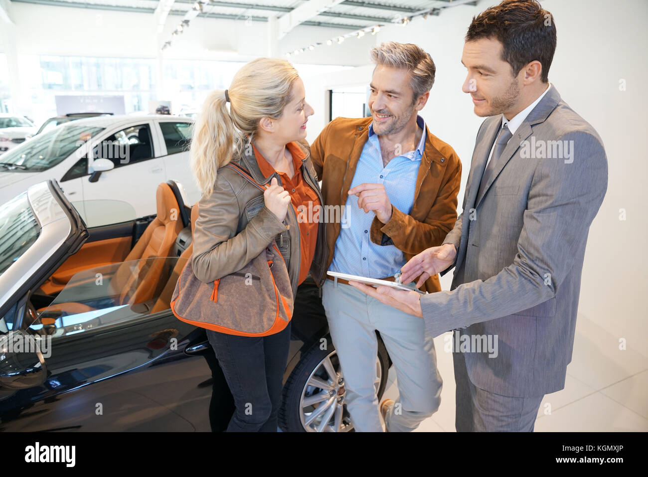 Car seller with couple in car dealership Stock Photo - Alamy