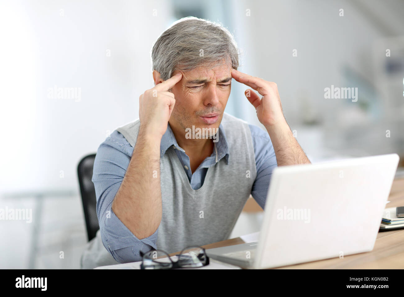 Senior businessman in front of laptop having a headache Stock Photo - Alamy