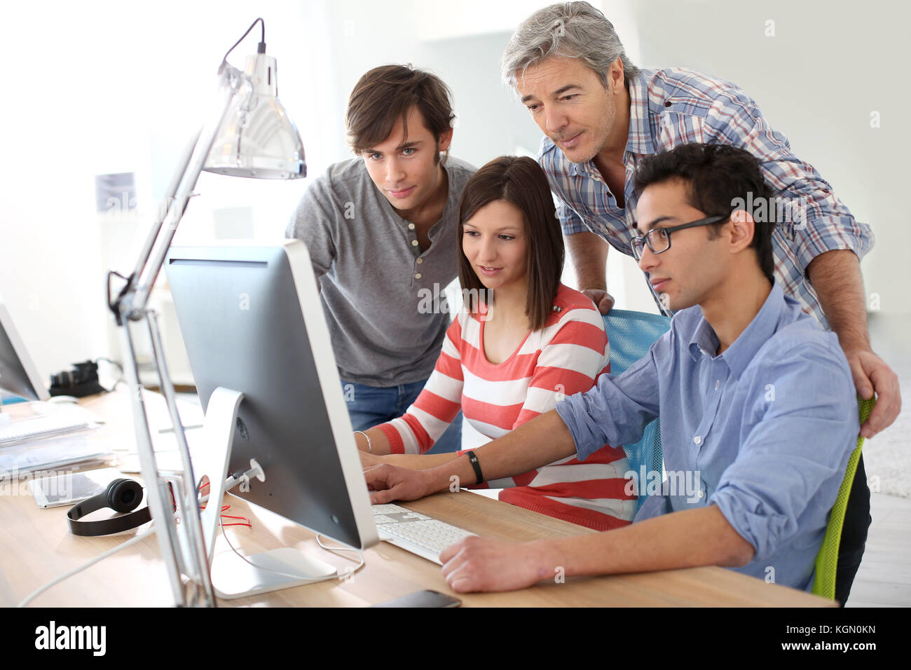 Teacher with students working on desktop Stock Photo - Alamy
