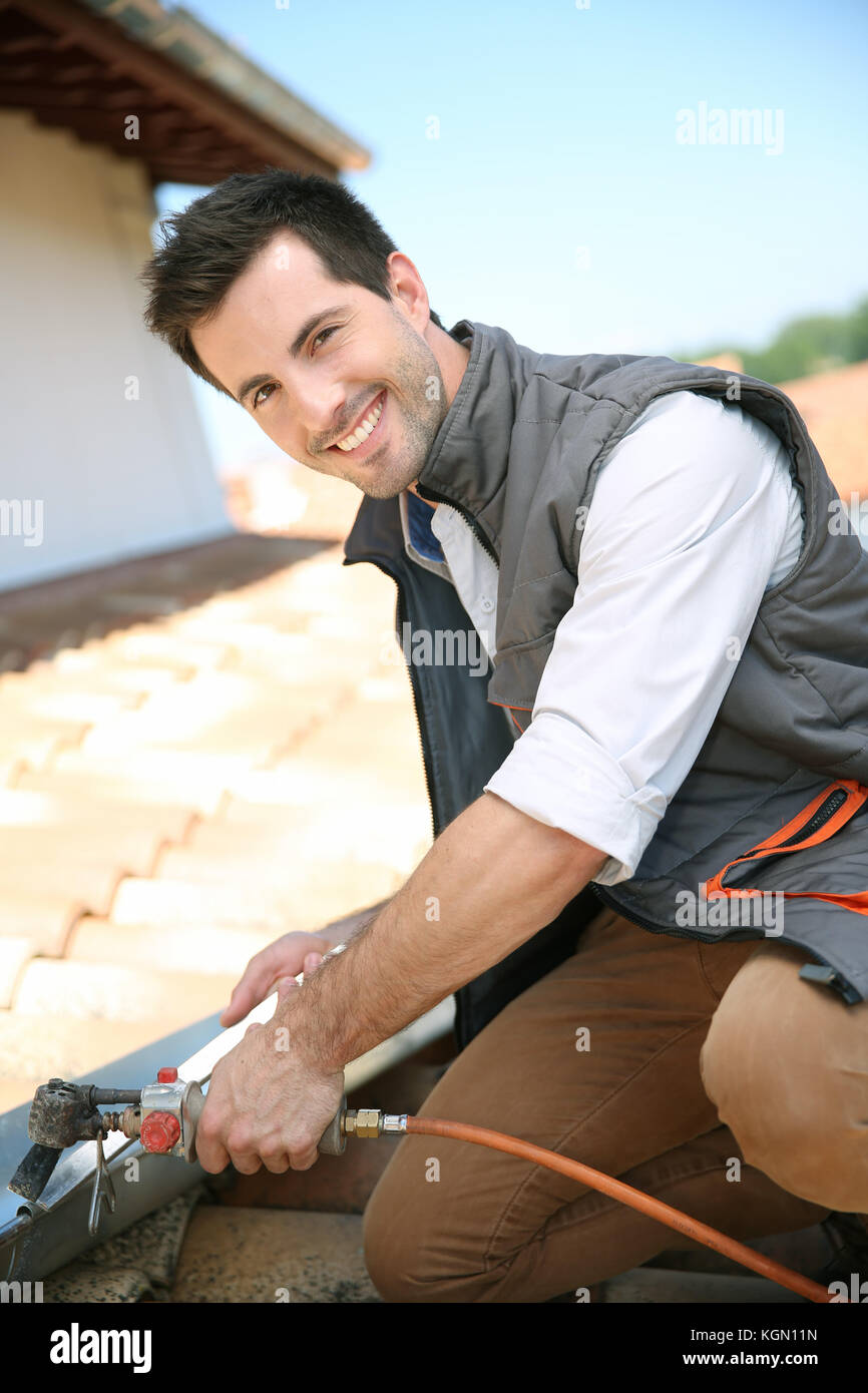 Roofer working on house roof to fix gutter Stock Photo - Alamy