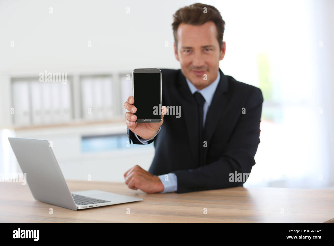 Businessman holding and showing smartphone towards camera Stock Photo ...