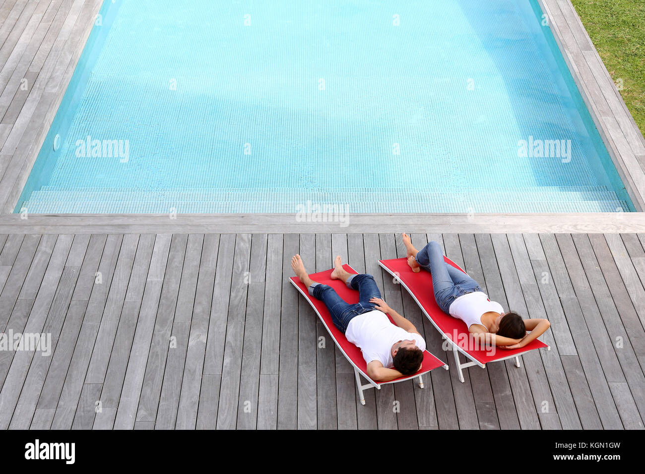 Couple relaxing in long chairs by outdoor pool Stock Photo - Alamy