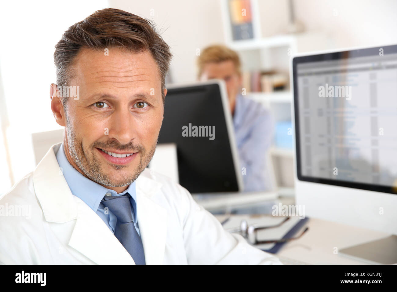 Portrait of smiling doctor sitting in front of computer Stock Photo - Alamy