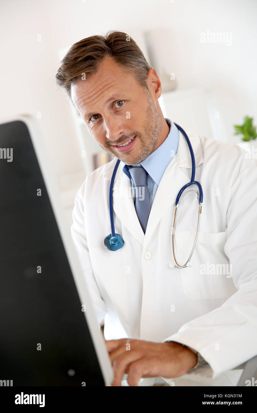 Portrait of smiling doctor sitting in front of computer Stock Photo - Alamy