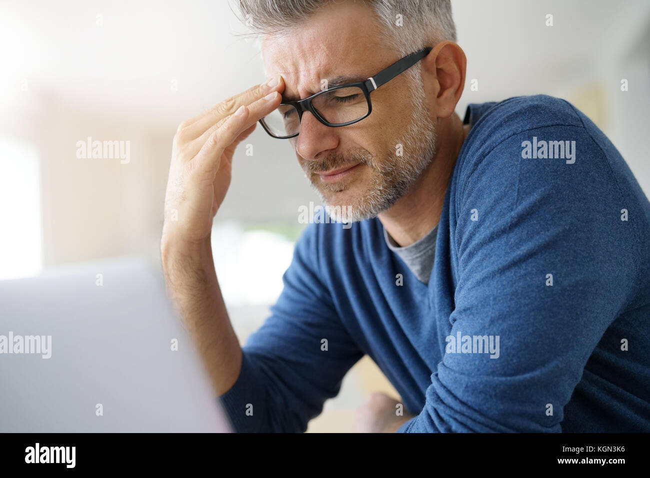 Man at home having a headache in front of laptop Stock Photo - Alamy