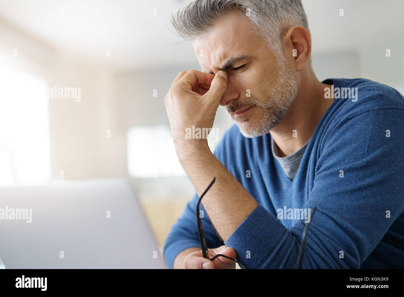 Man at home having a headache in front of laptop Stock Photo - Alamy