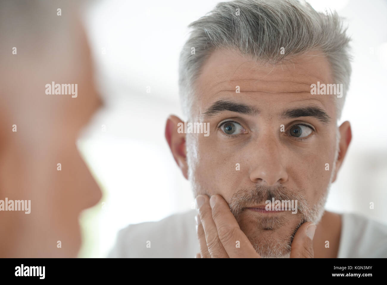 Middle-aged man applying cosmetic on his face, mirror view Stock Photo ...