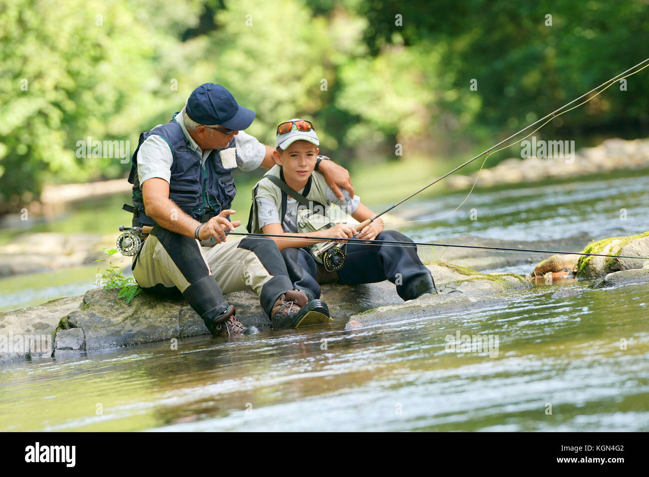 Father and son fly-fishing in river, sitting on rocks Stock Photo - Alamy