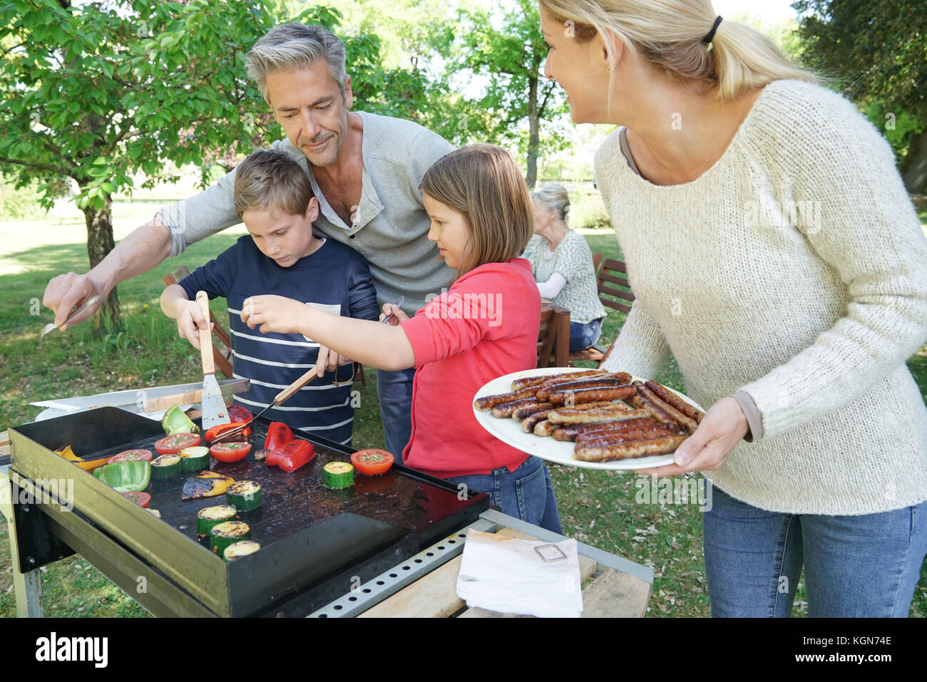 Family preparing grilled meet on barbecue Stock Photo - Alamy