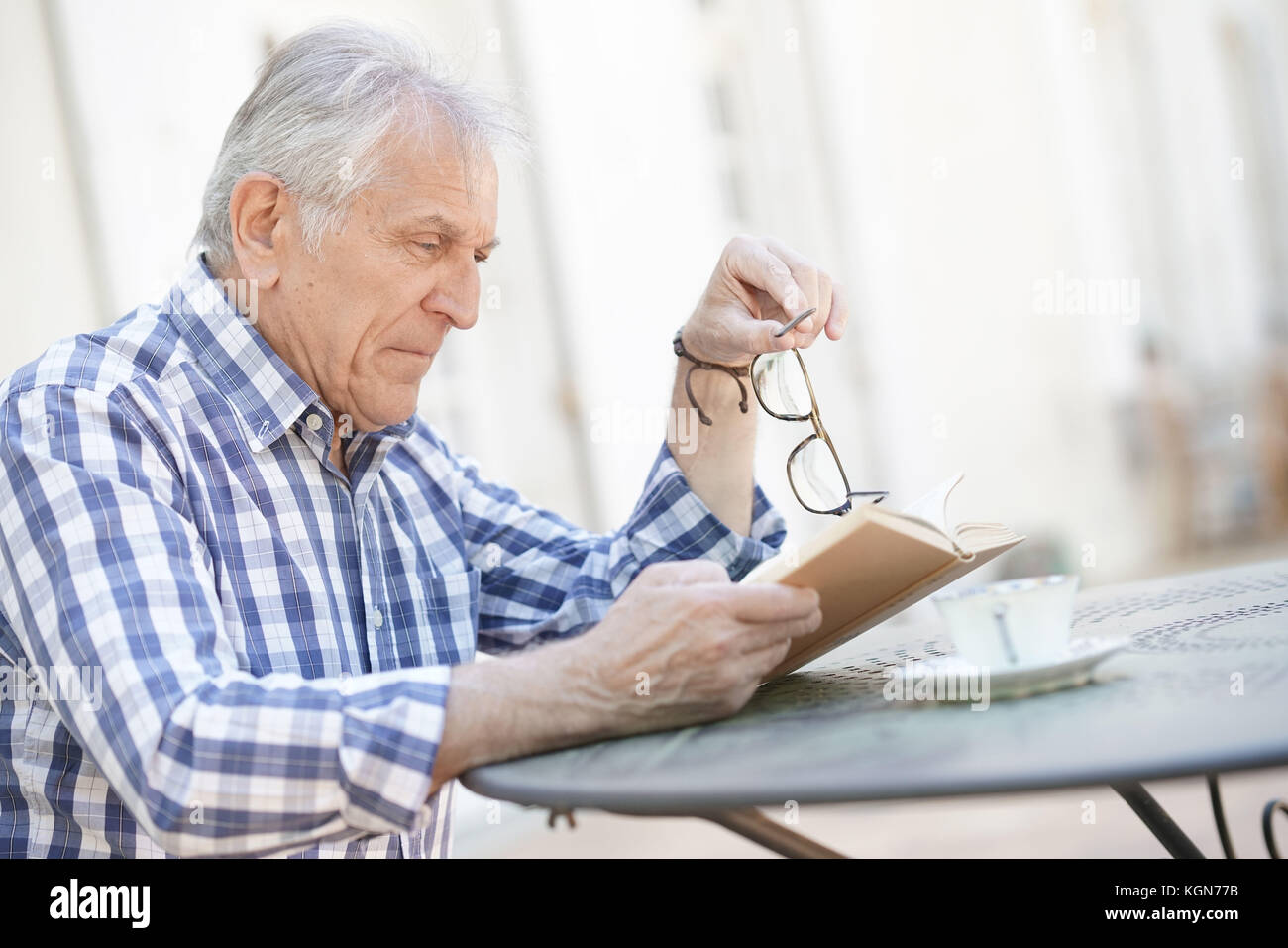 Elderly man with eyeglasses reading book outside Stock Photo - Alamy