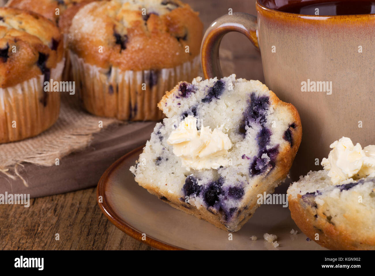 Closeup of a sliced blueberry muffin and butter with a cup of coffee ...