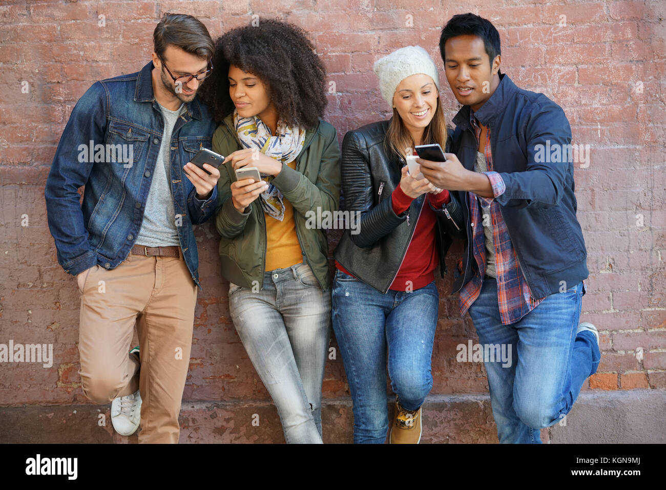 Friends leaning on brick wall, playing with smartphones Stock Photo - Alamy